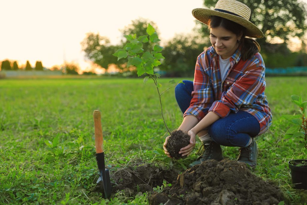 Young woman planting tree in countryside | Blain's Farm & Fleet Blog